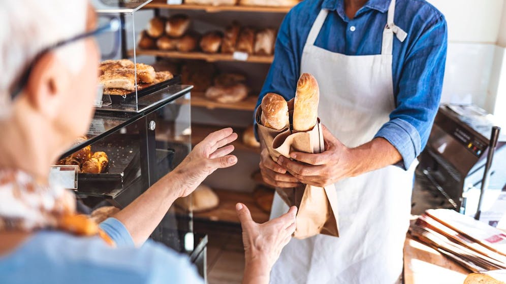 Cropped shot of a male baker wearing apron giving paper shopping bag to ...